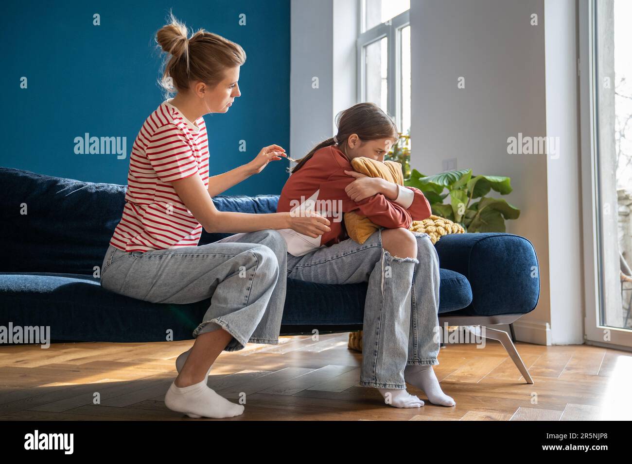 Caring mother cuddles teenage girl sitting on sofa and hug pillow ...