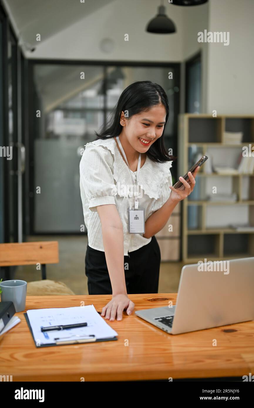 Portrait of an attractive and happy Asian businesswoman or female manager bending over table and ...