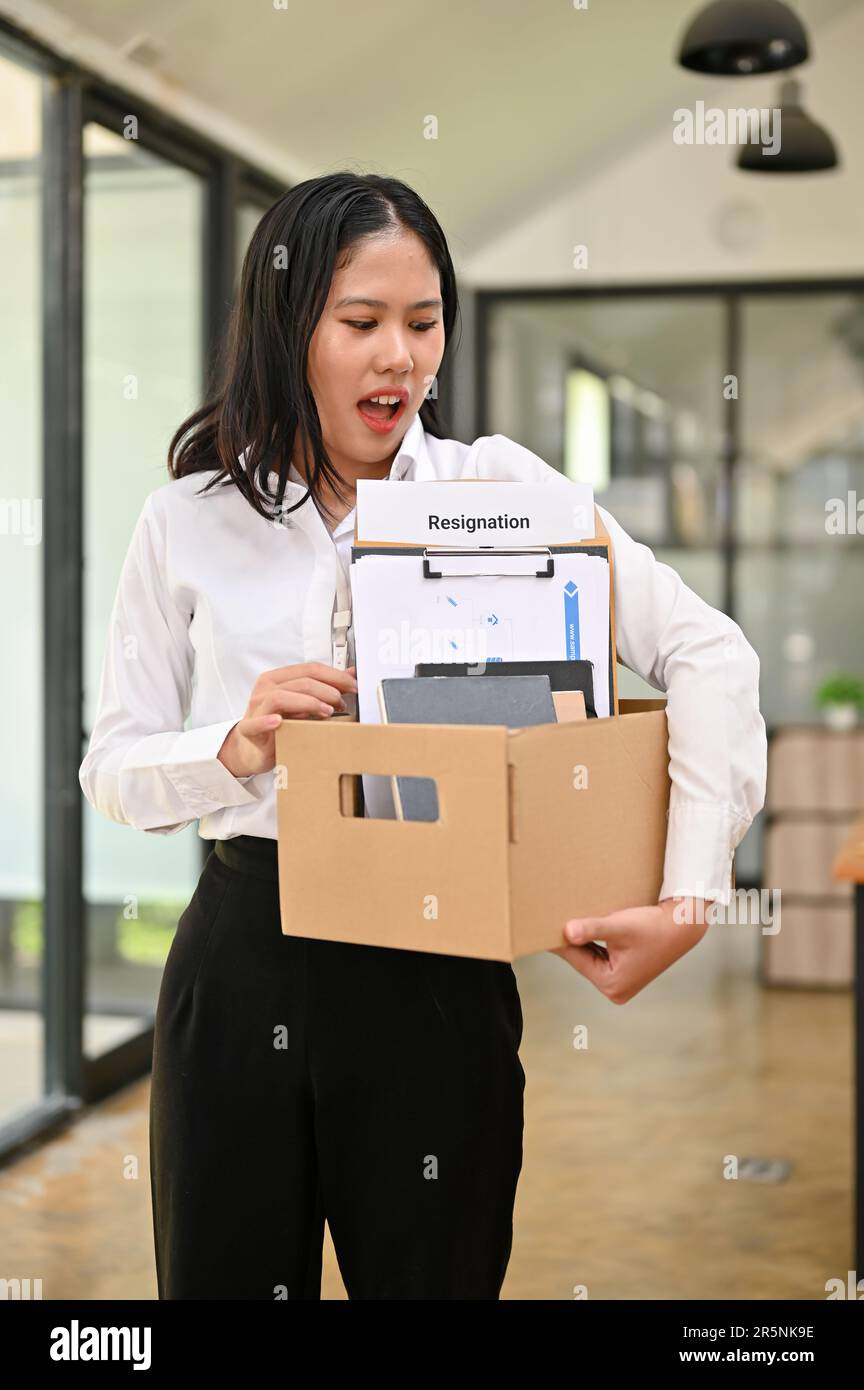 Excited young Asian female office worker carrying her belonging ...
