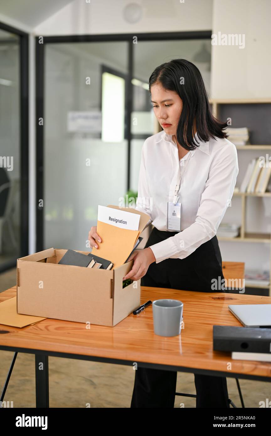 A sad and frustrated young Asian female office worker packing her stuff ...