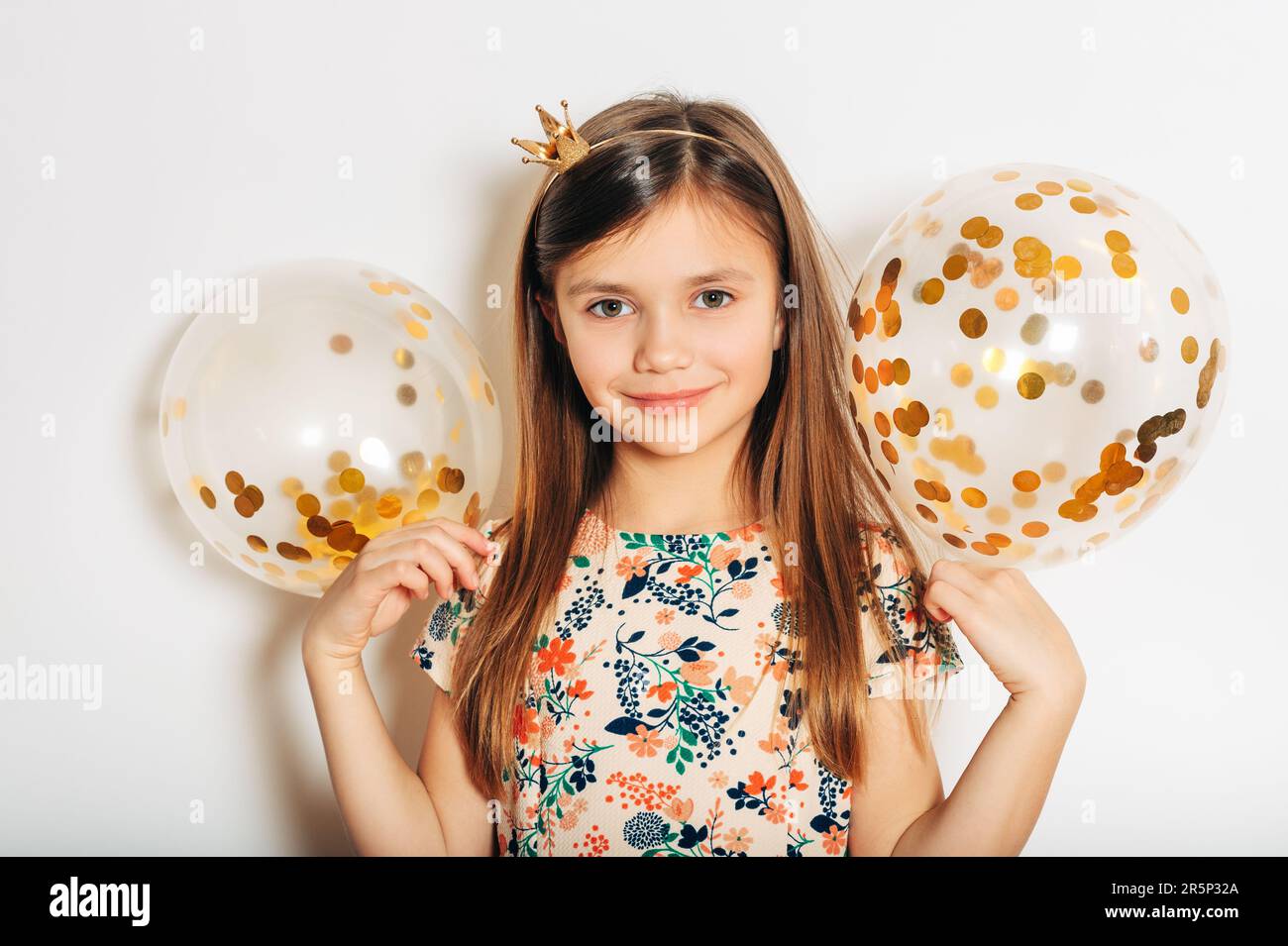 Studio portrait of cute little girl holding helium balloons with golden ...