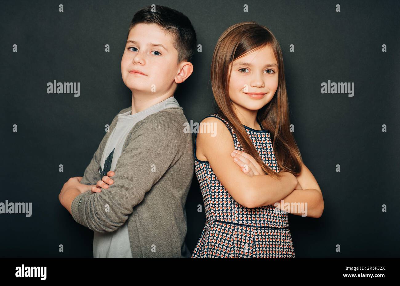 Studio portrait of two cute kids, standing back to back, arms crossed ...