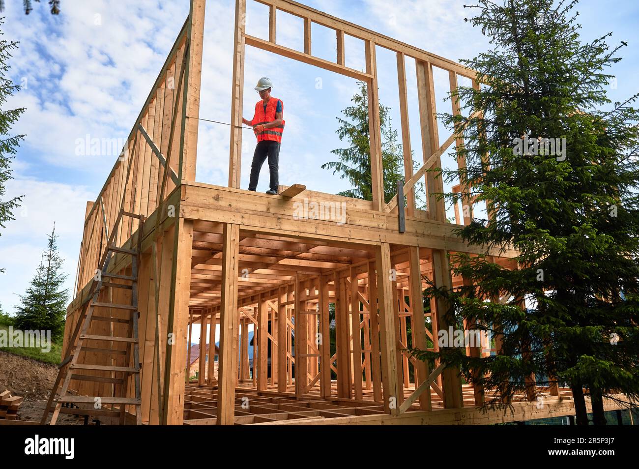 Carpenter constructing timber-framed two-story building. Man measures ...