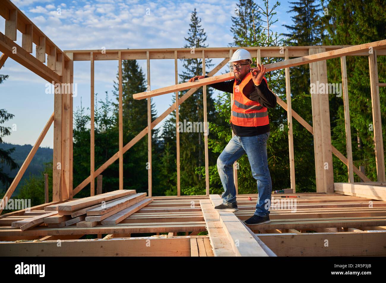 Carpenter constructing wooden-framed house near woods. Man holding ...