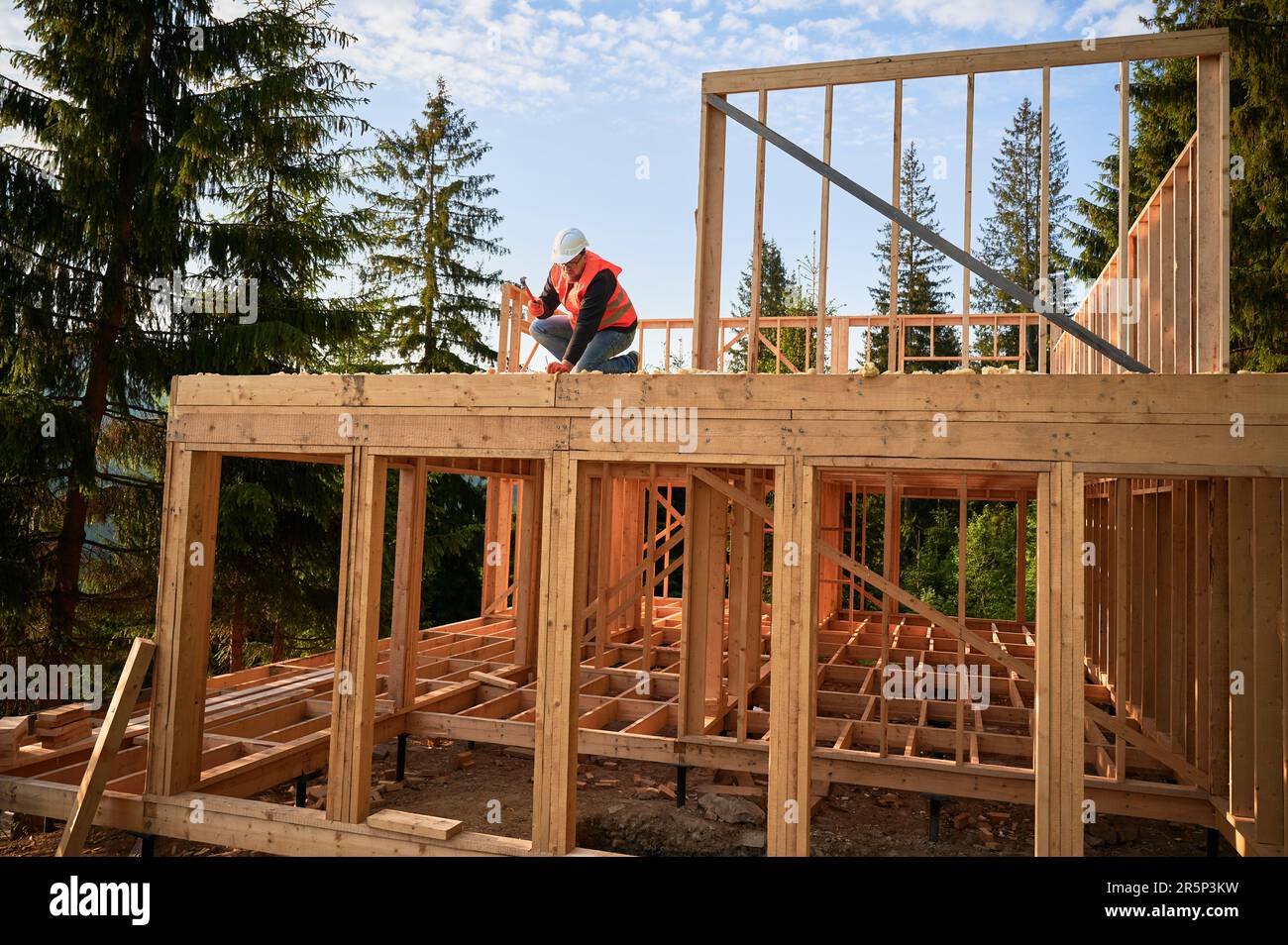 Carpenter constructing two-story wooden frame house near forest ...