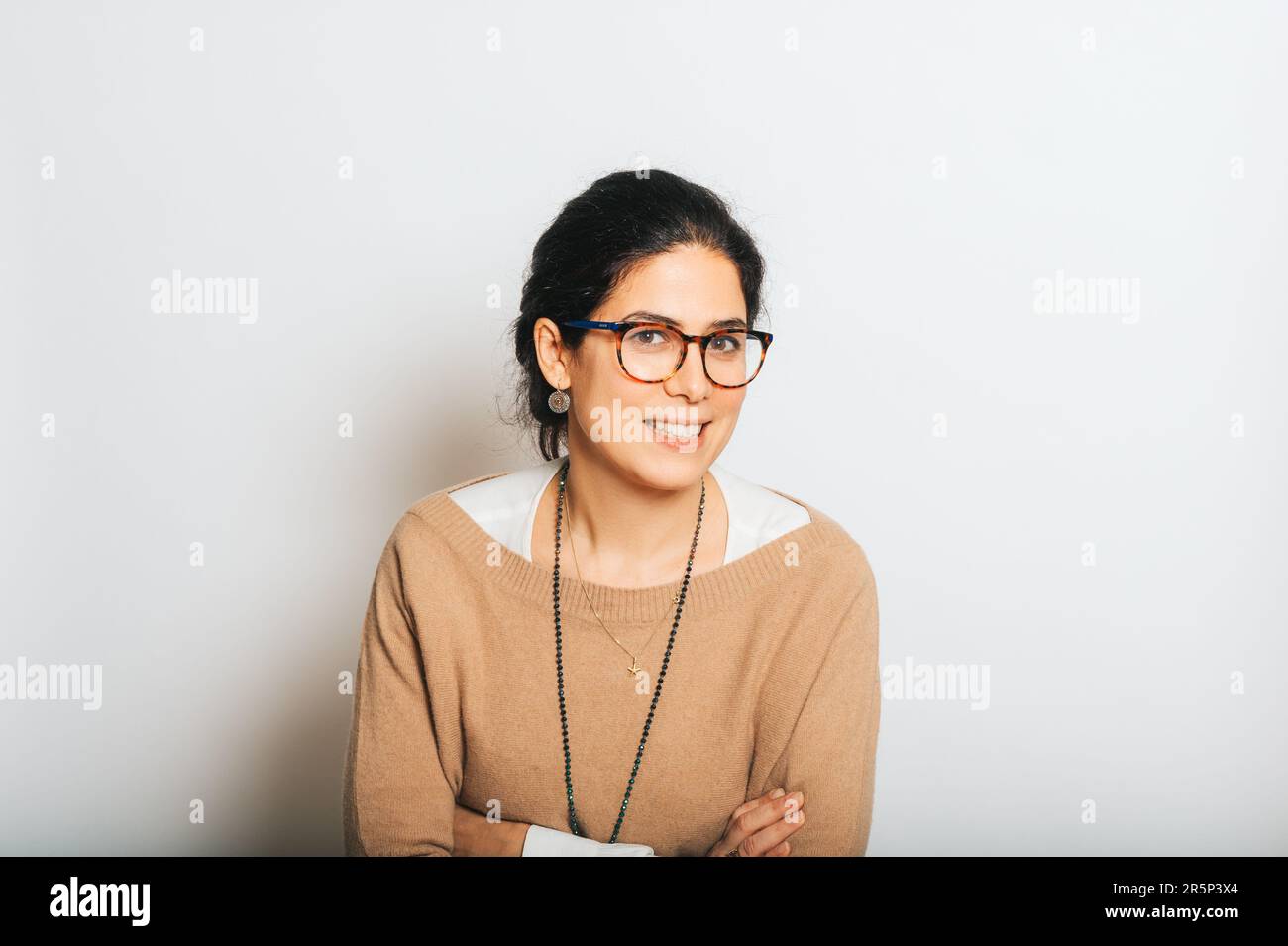 Studio portrait of beautiful brunette woman, wearing glasses, arms ...