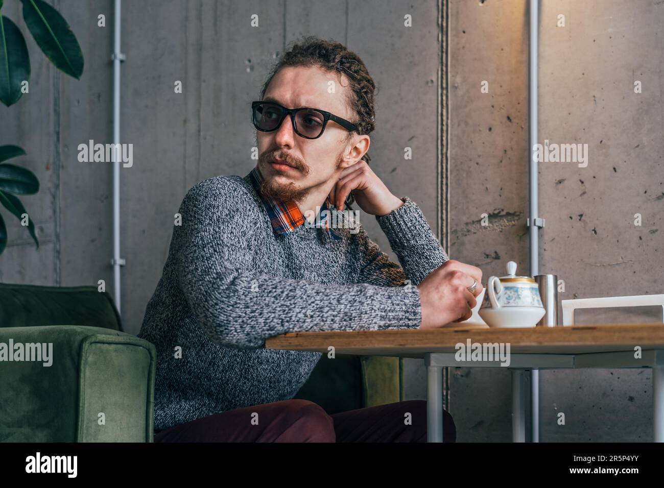 Alone young man in glasses sit in cafe, turning around as if he is ...