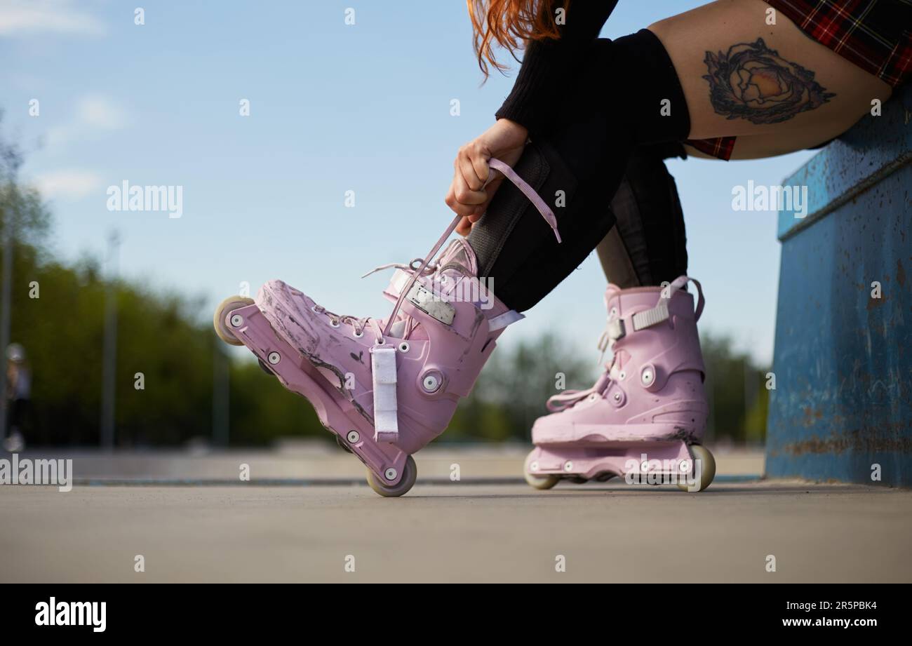 Aggressive inline skater girl tying laces on modern roller blades in a ...