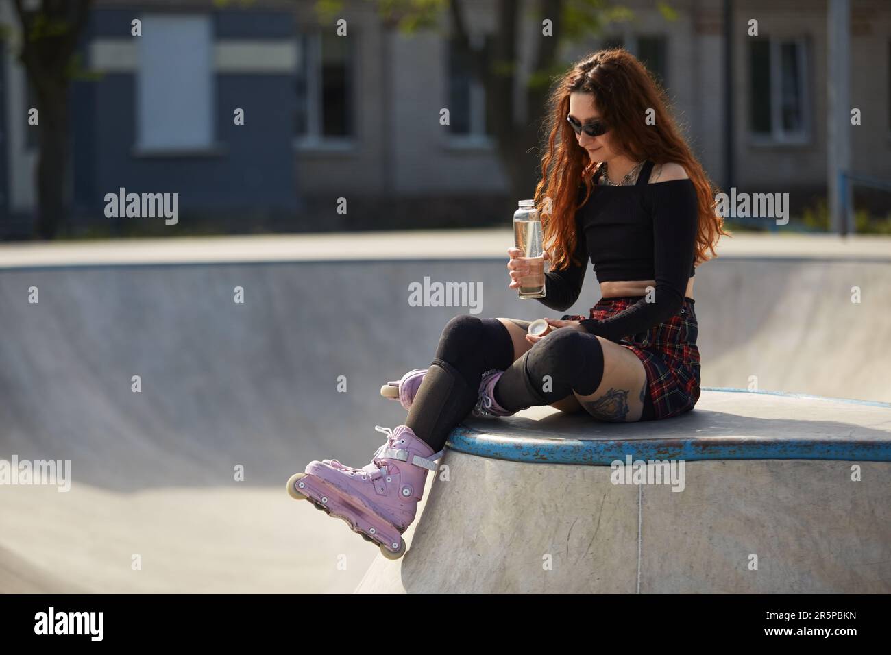 Roller blader female sitting on a ramp top in a skate park with a glass ...
