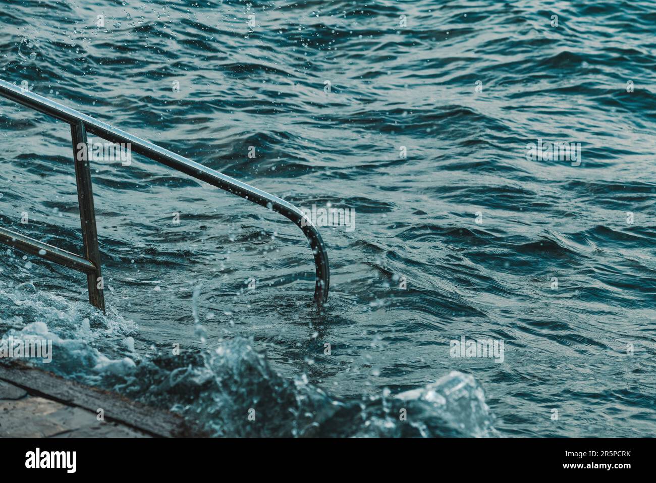 Ocean water waves breaking at the shoreline over metallic railing Stock ...