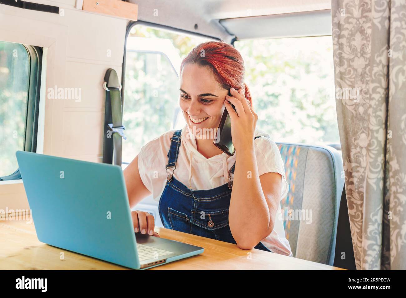 Young woman using her laptop and having a phone call inside her camper ...