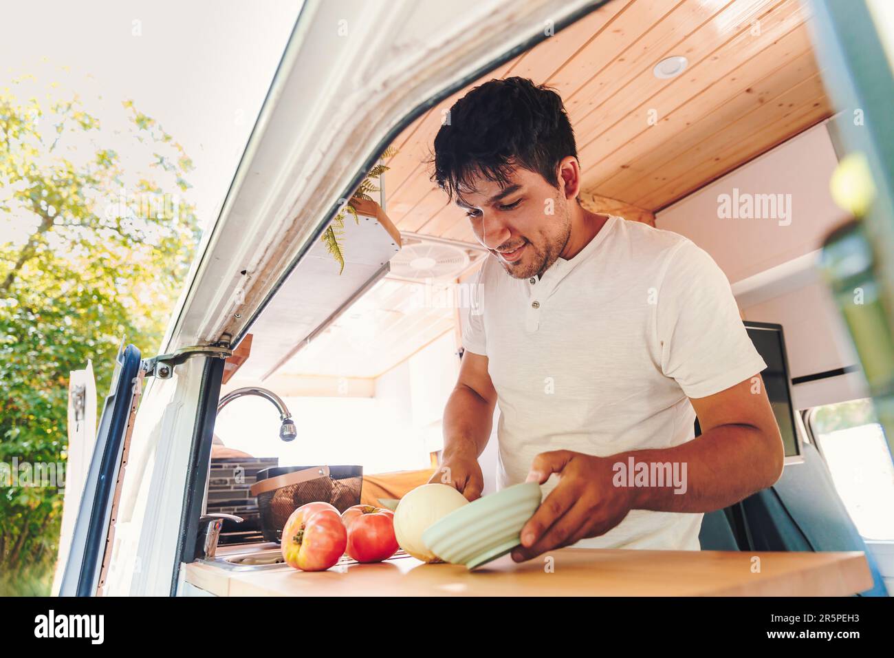 Young latin man cooking food in the kitchen of his handmade camper van ...