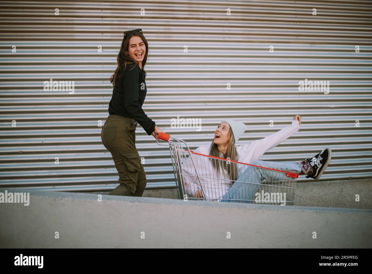 Two pretty girls having fun with a market cart at the garage Stock ...