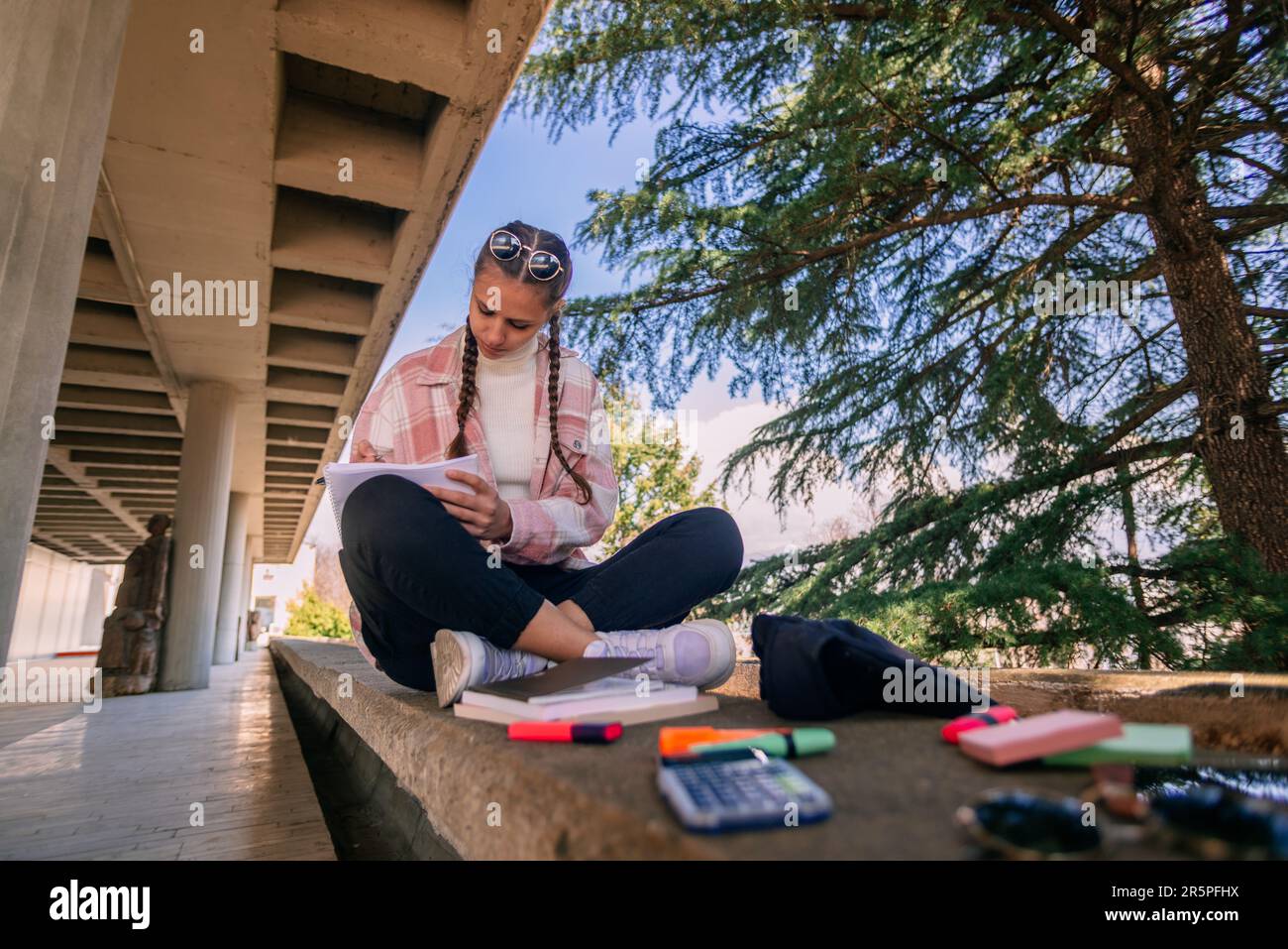 School girl writing homework while sitting on a ledge. Low angle view ...