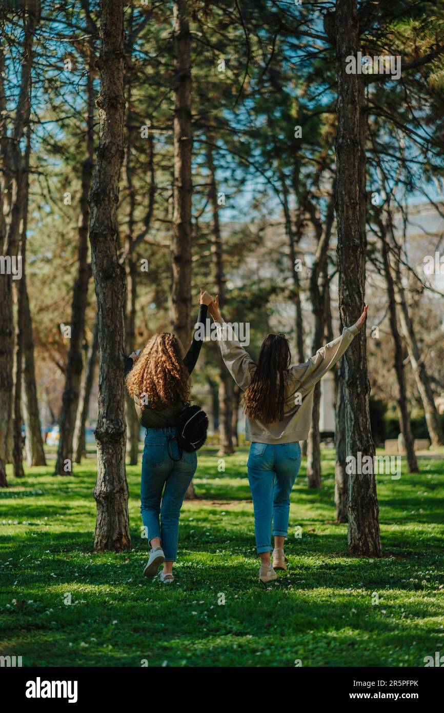Back view shot of two girls holding their hands up and jump while ...