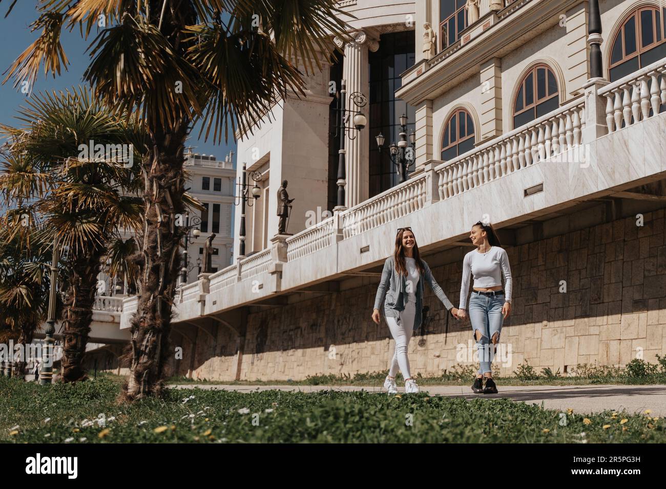Two pretty girls walking at the park in front of the buildings while ...