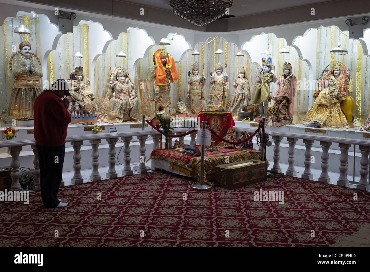 A male worshipper bows in front of a row several statues of deities ...