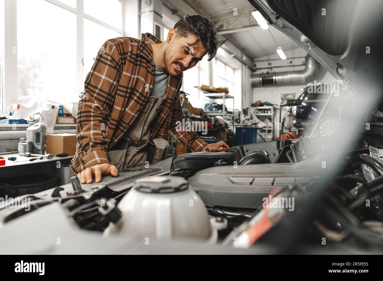 Young male mechanic examining engine under hood of car at the repair ...