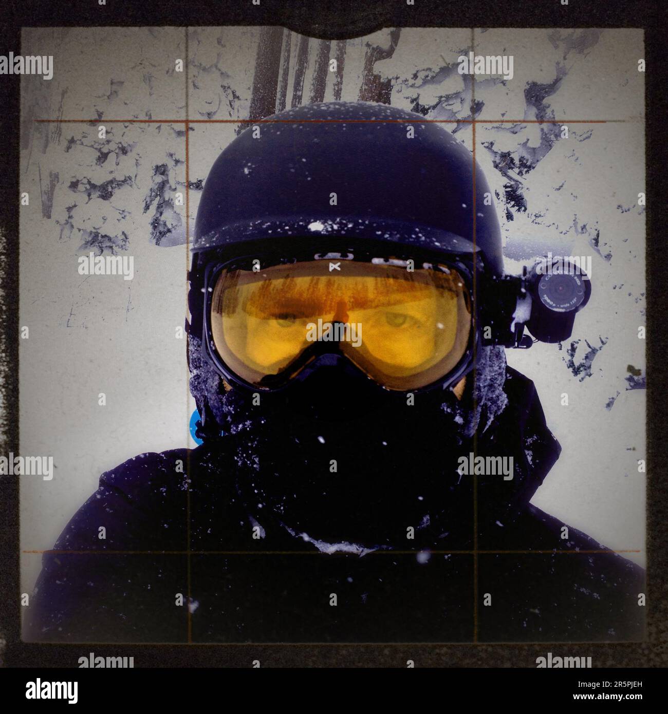 Portrait of a snowboarder wearing a helmet and yellow goggles. His face is obscured by a mask ...