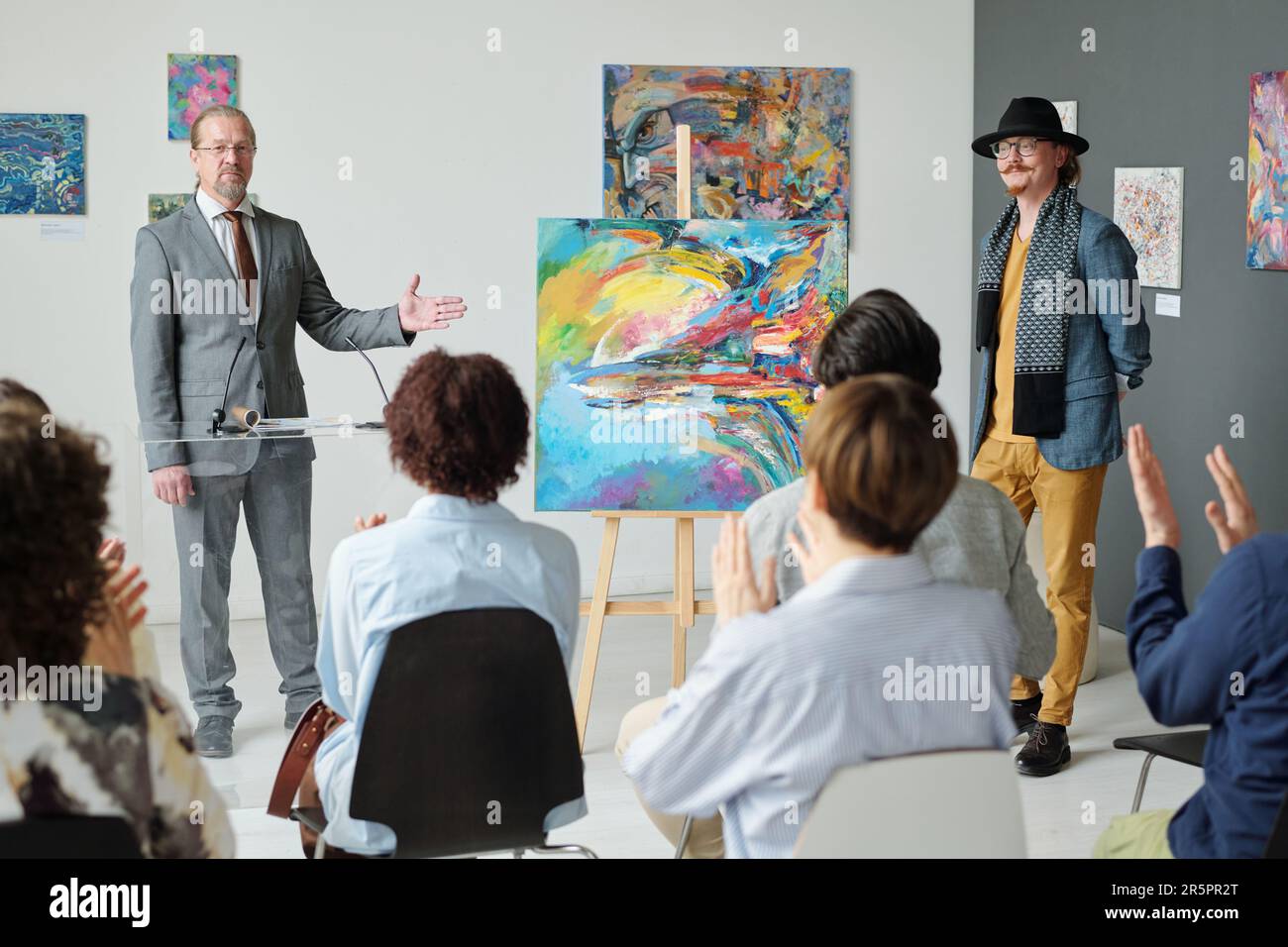 Man in suit presenting the painting of artist to group of people during ...
