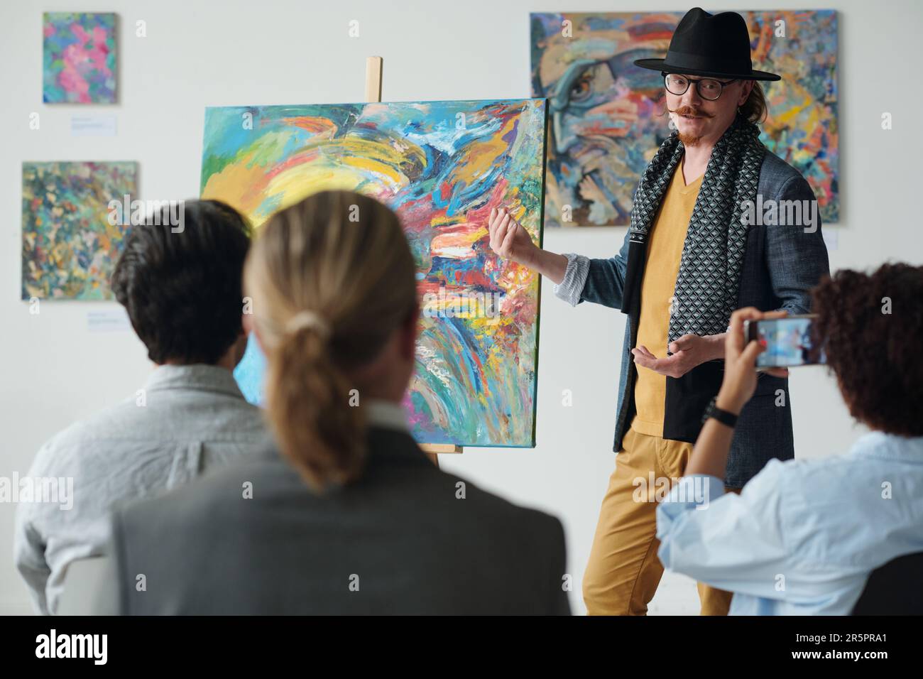 Artist in elegant clothing presenting his picture on canvas to group of ...