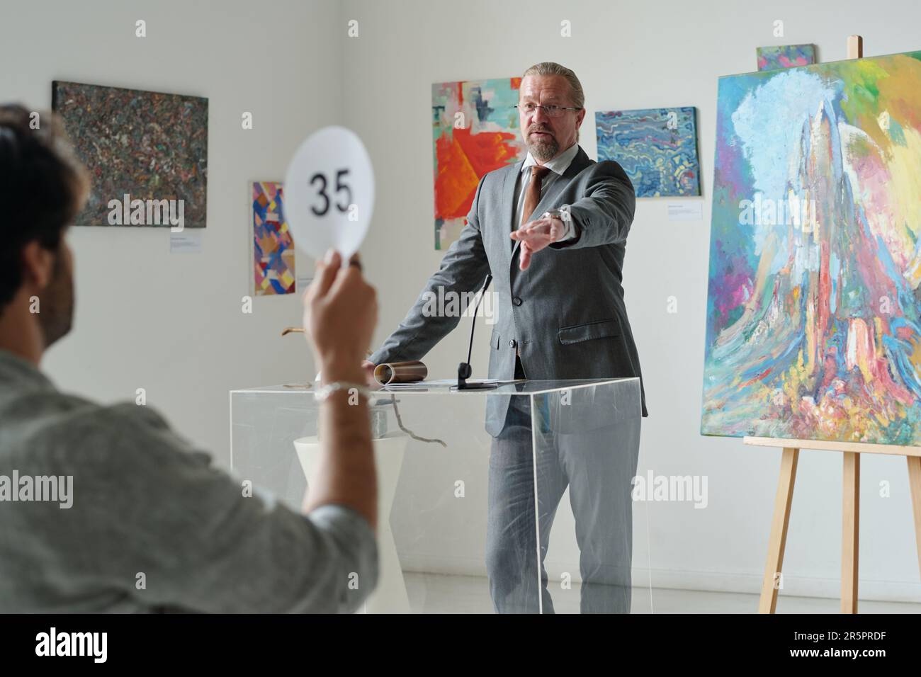 Mature man in suit holding auction about modern painting in art gallery ...