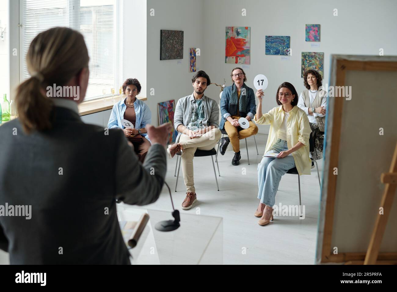 Group of people sitting at auction in art gallery and buying painting ...