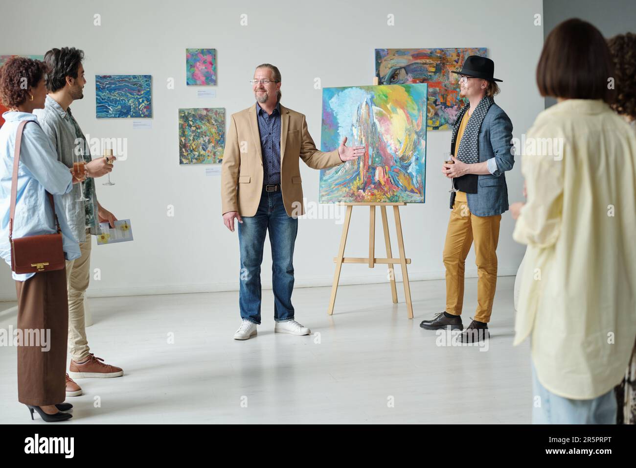 Gallery owner presenting modern art of artist to group of people during ...