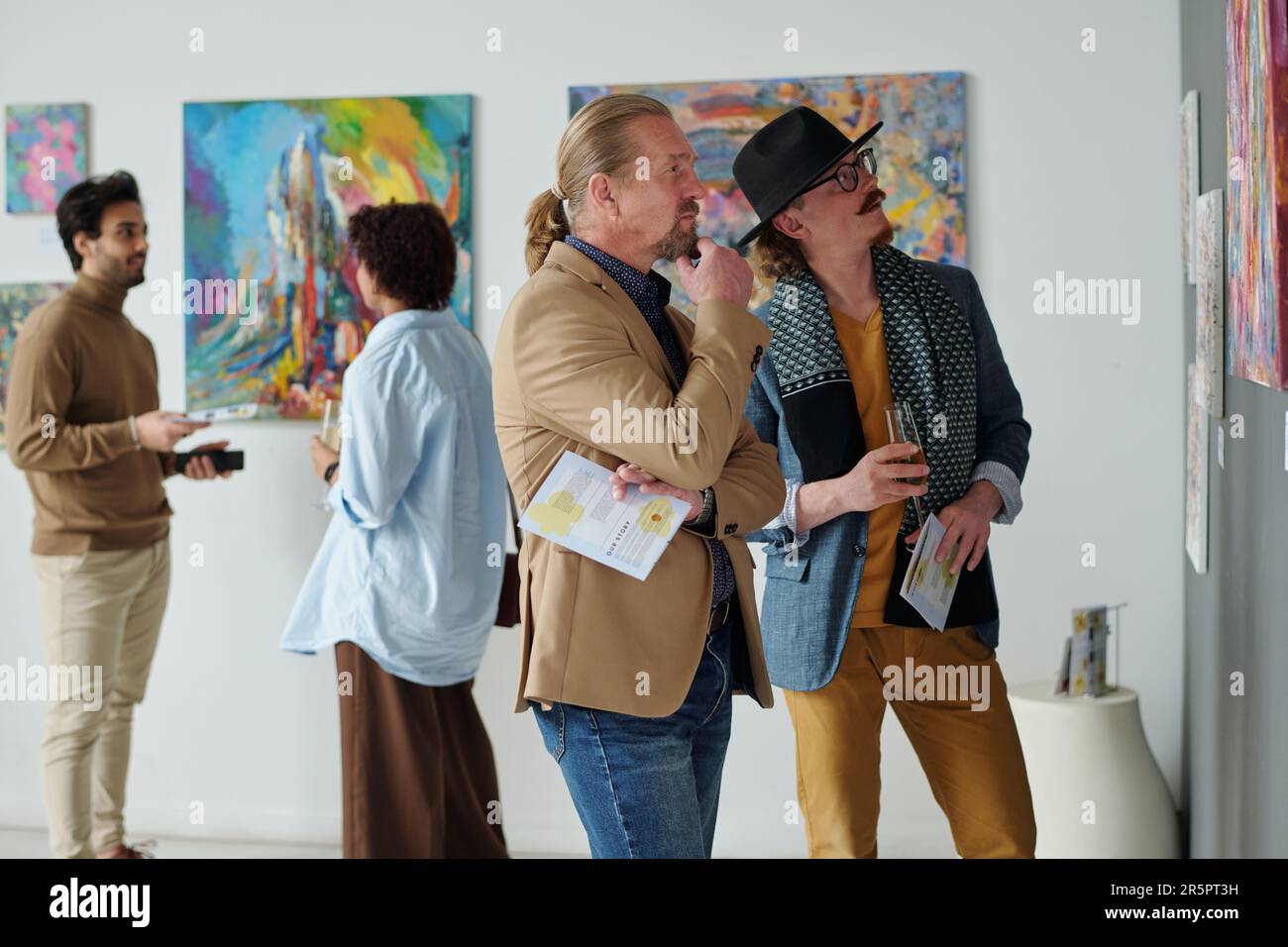 People looking at paintings on the wall and discussing them while ...