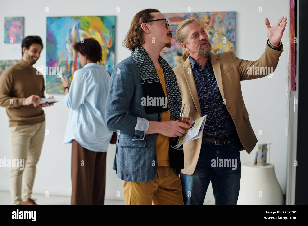 Art lovers discussing modern art in gallery, they pointing at wall with ...