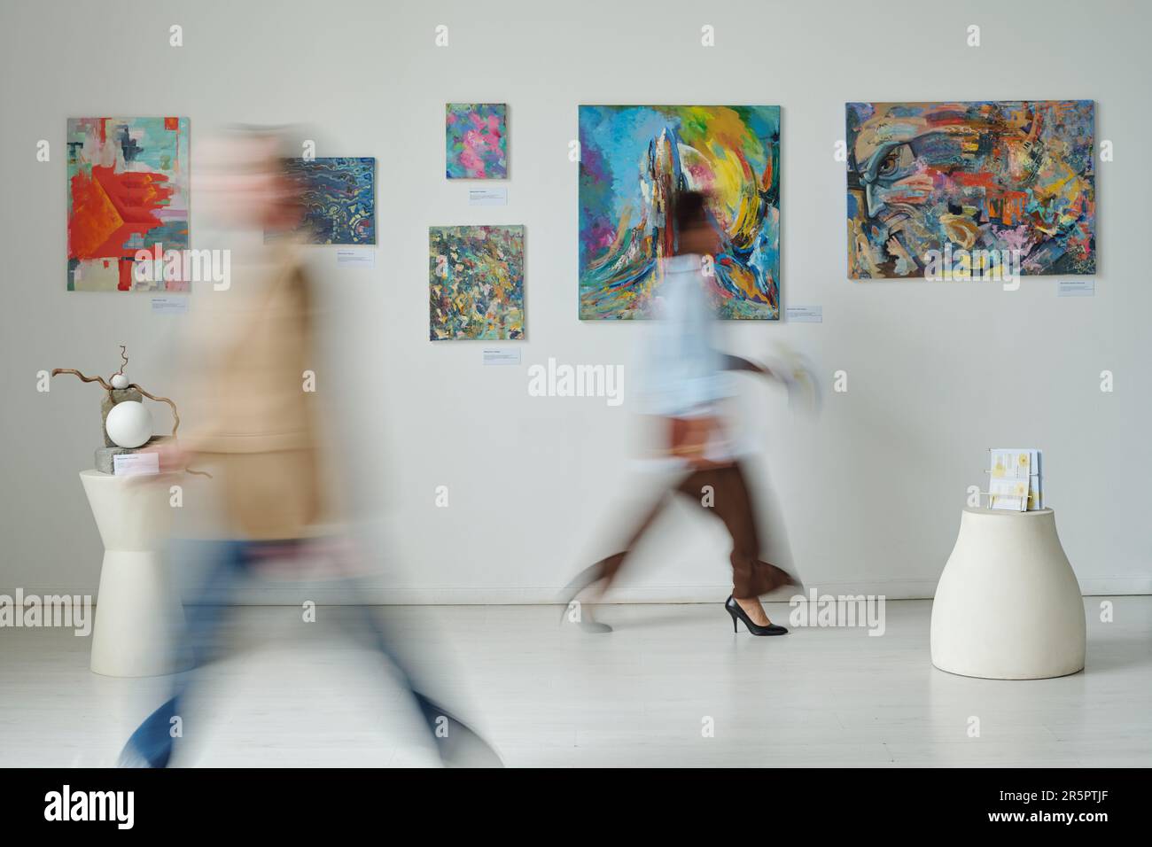Blurred motion of people passing through the paintings on the wall in ...