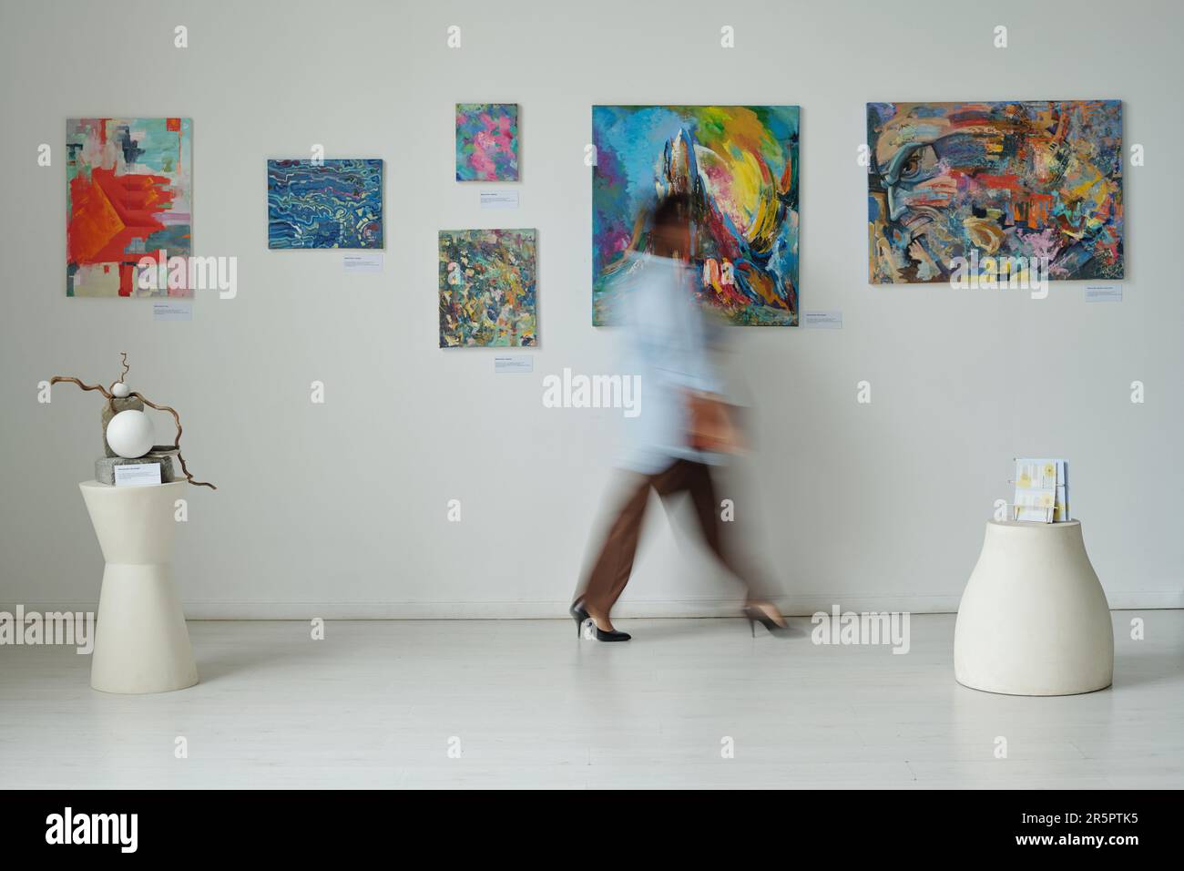 Blurred motion of young woman walking through paintings on the wall in ...