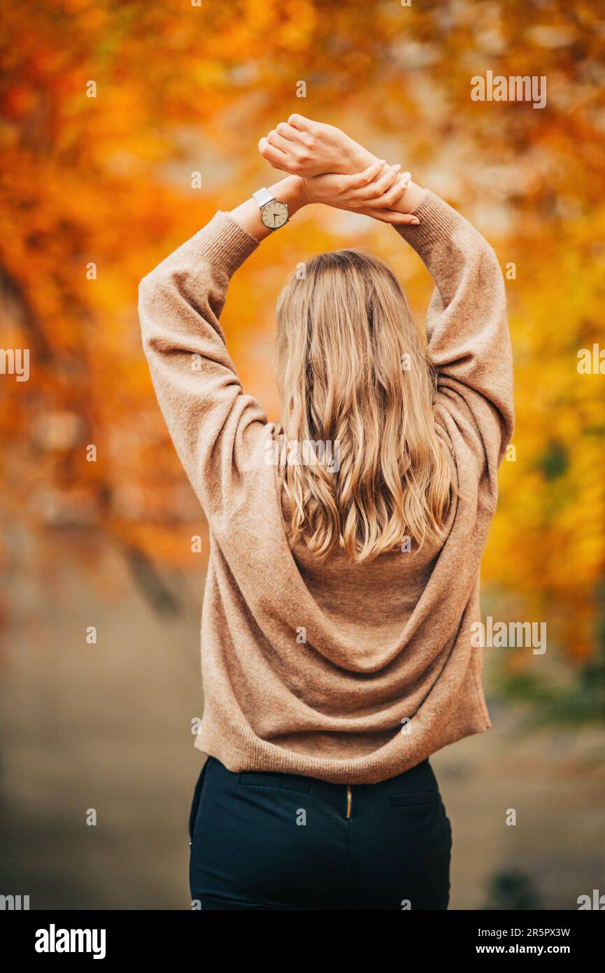 Outdoor portrait of young blonde woman admiring golden leaves, holding ...