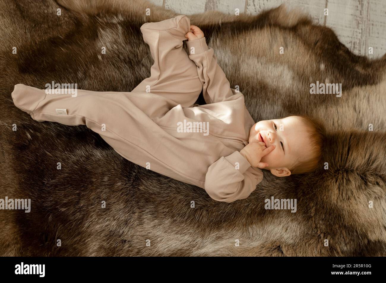 An Asian child, holding his leg with hand, lies on back on a warm deer ...