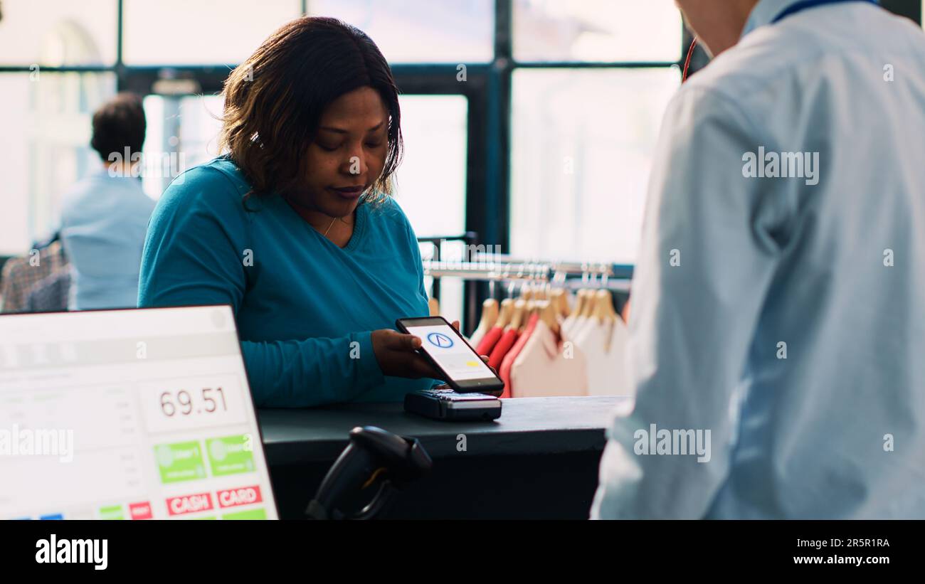 African american client paying for casual wear with mobile phone nfc on ...