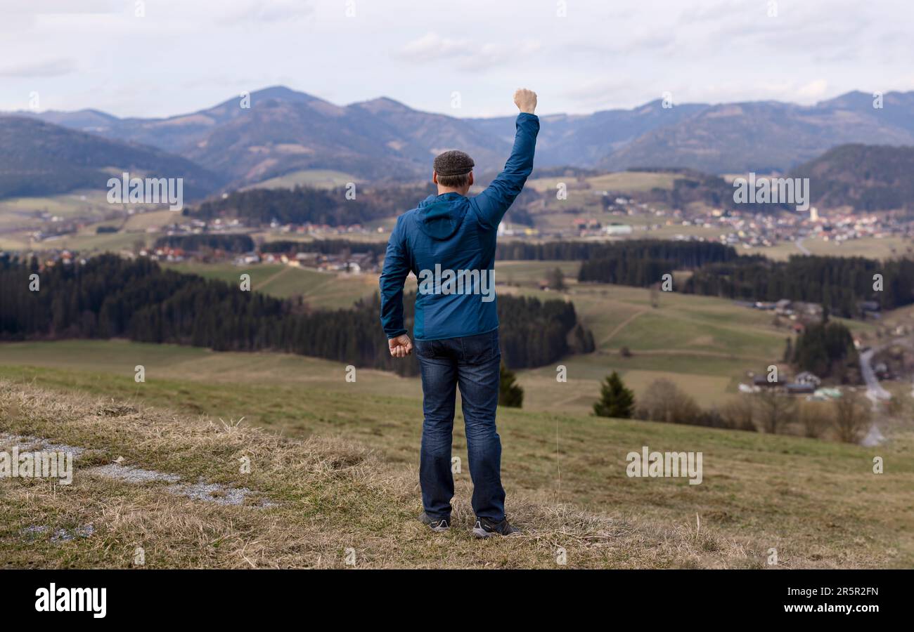 a man waves his hand, standing on a hill against the beautiful alpine ...
