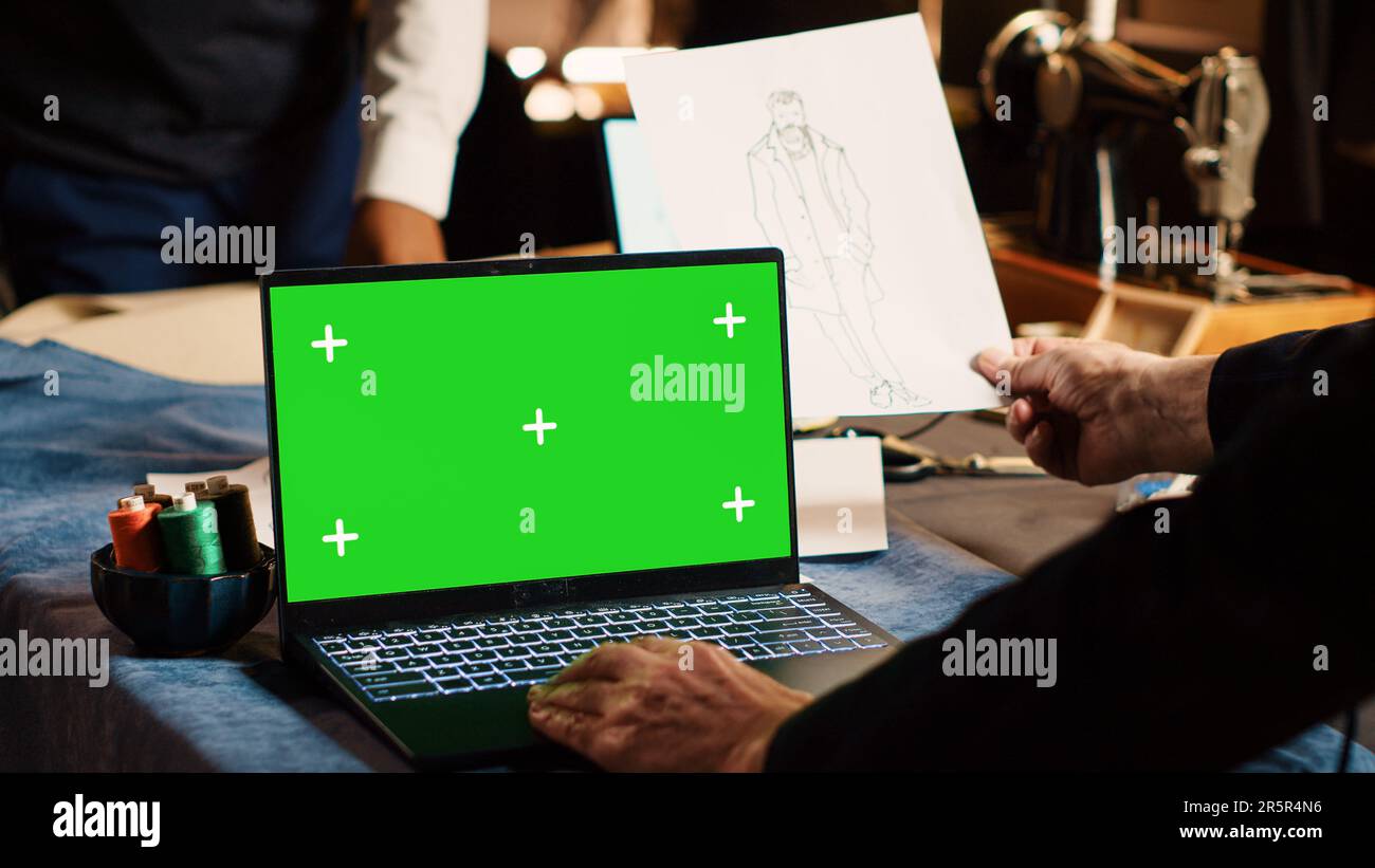 Craftsman using greenscreen on laptop, experienced tailor looking at ...