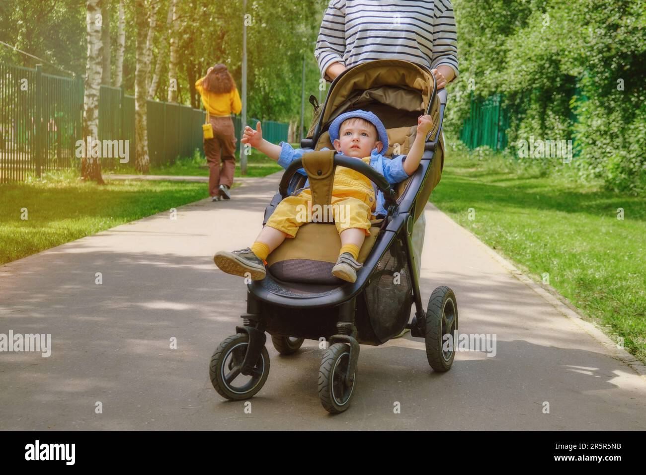 Mother with a baby boy in a pram is enjoying the sunny weather at the ...