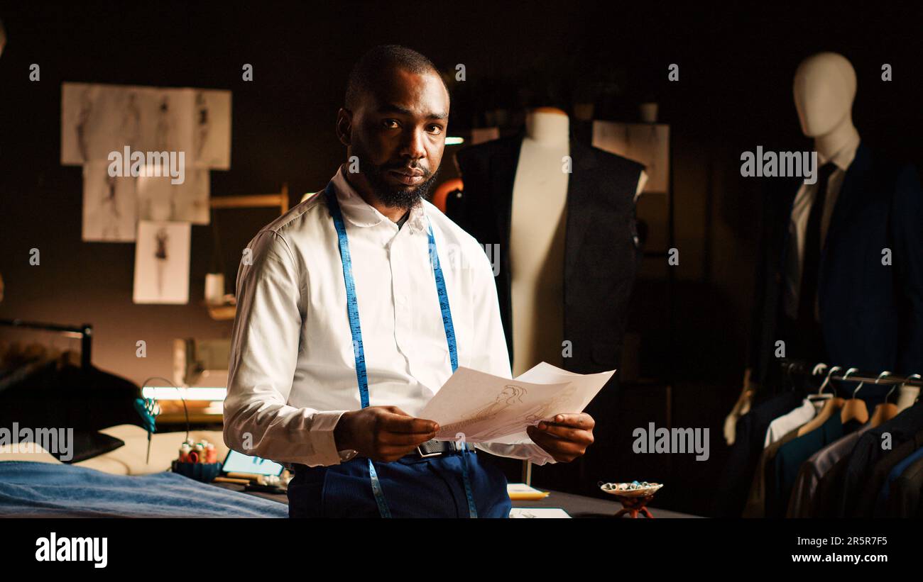 Male tailor checking sketches in atelier, using drawings of clothes and ...