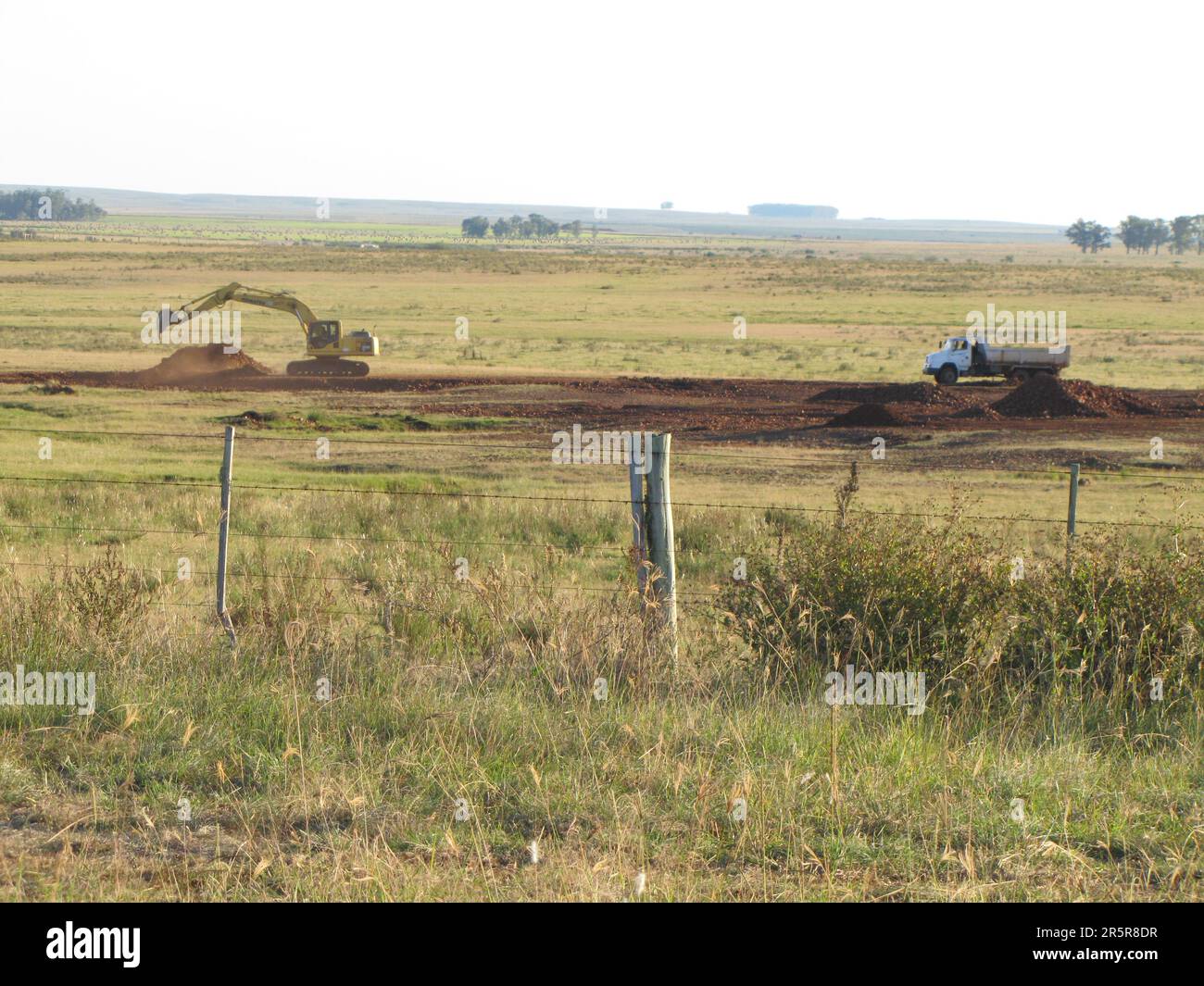 A backhoe and truck on the field digging the ground Stock Photo - Alamy