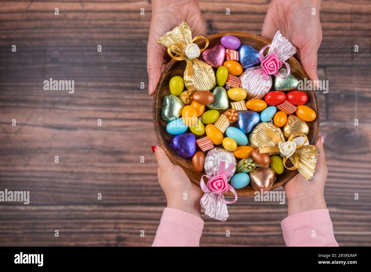 Holding bowl of chocolate candies. Wooden background, copy space ...