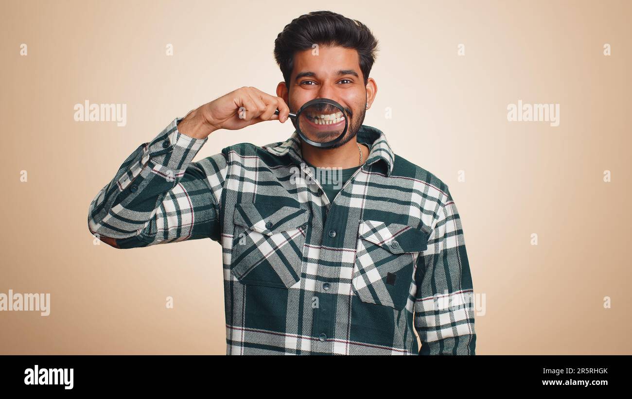 Indian man holding magnifier glass on healthy white teeth, looking at ...