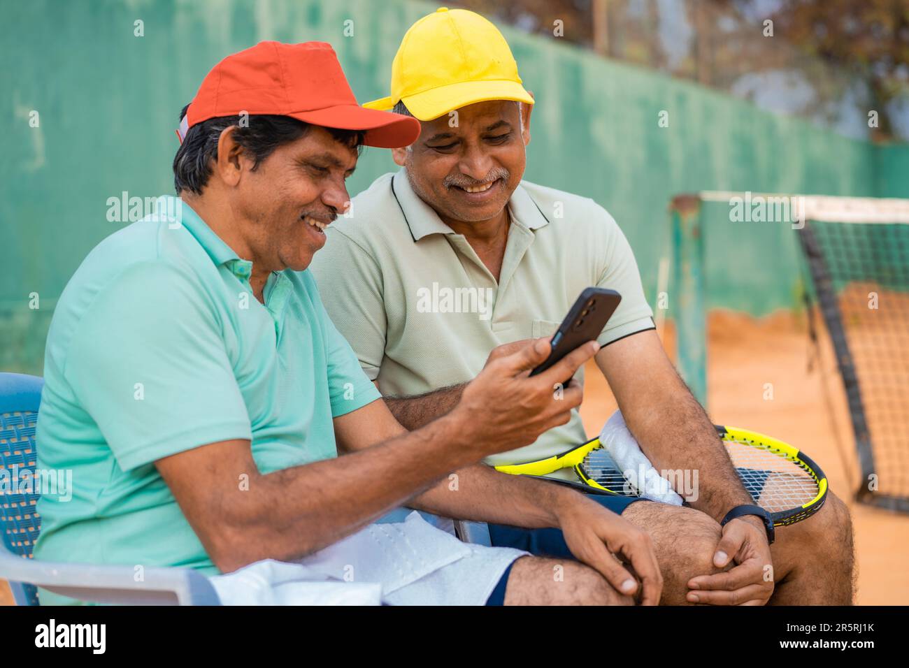 Happy smiling senior friends watching mobile phone after playing tennis ...