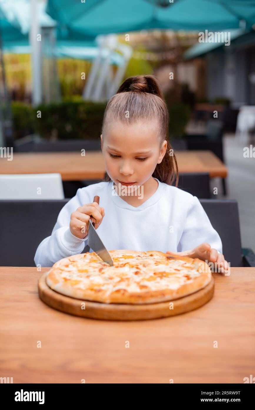 Hungry kid girl eating pizza on cafe terrace. outside restaurant copy ...