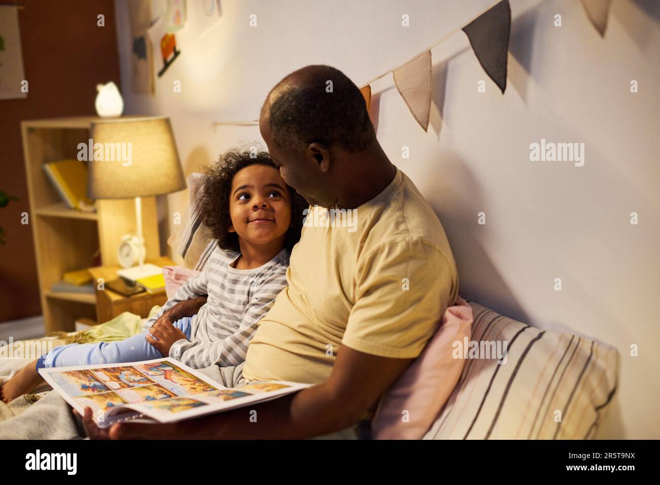 African American dad reading tale to his child before sleep, they ...
