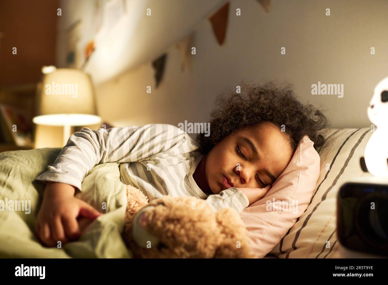 Cute African American little boy sleeping in bed with toy at night ...