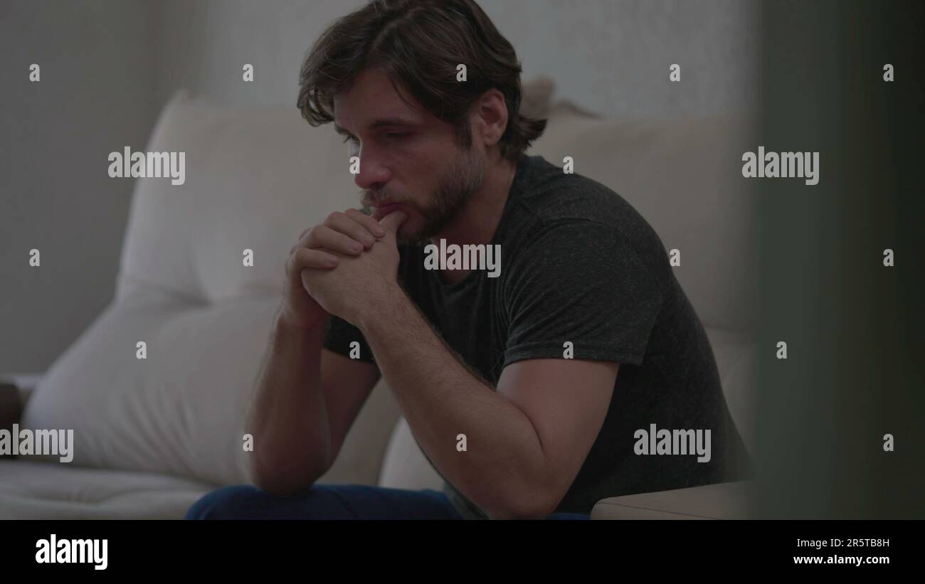 One contemplative pensive young man sitting on couch at home with ...