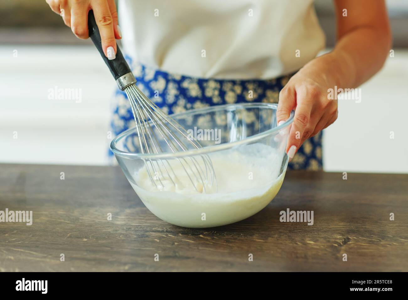 Beautiful hands stir the dough with a black whisk in a deep transparent ...