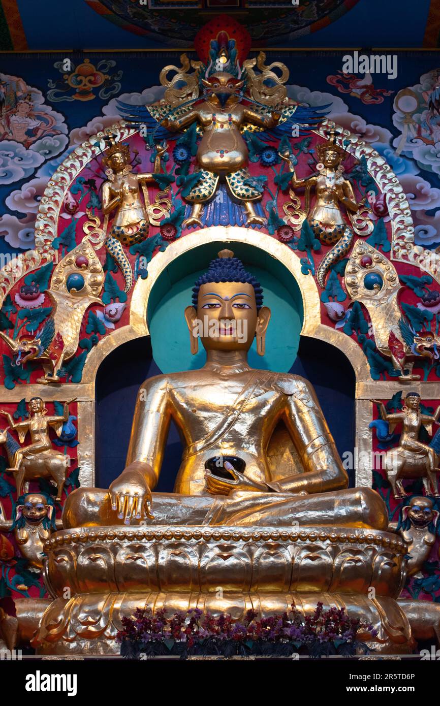 A large golden statue of the Buddha sitting in front of a wall covered ...