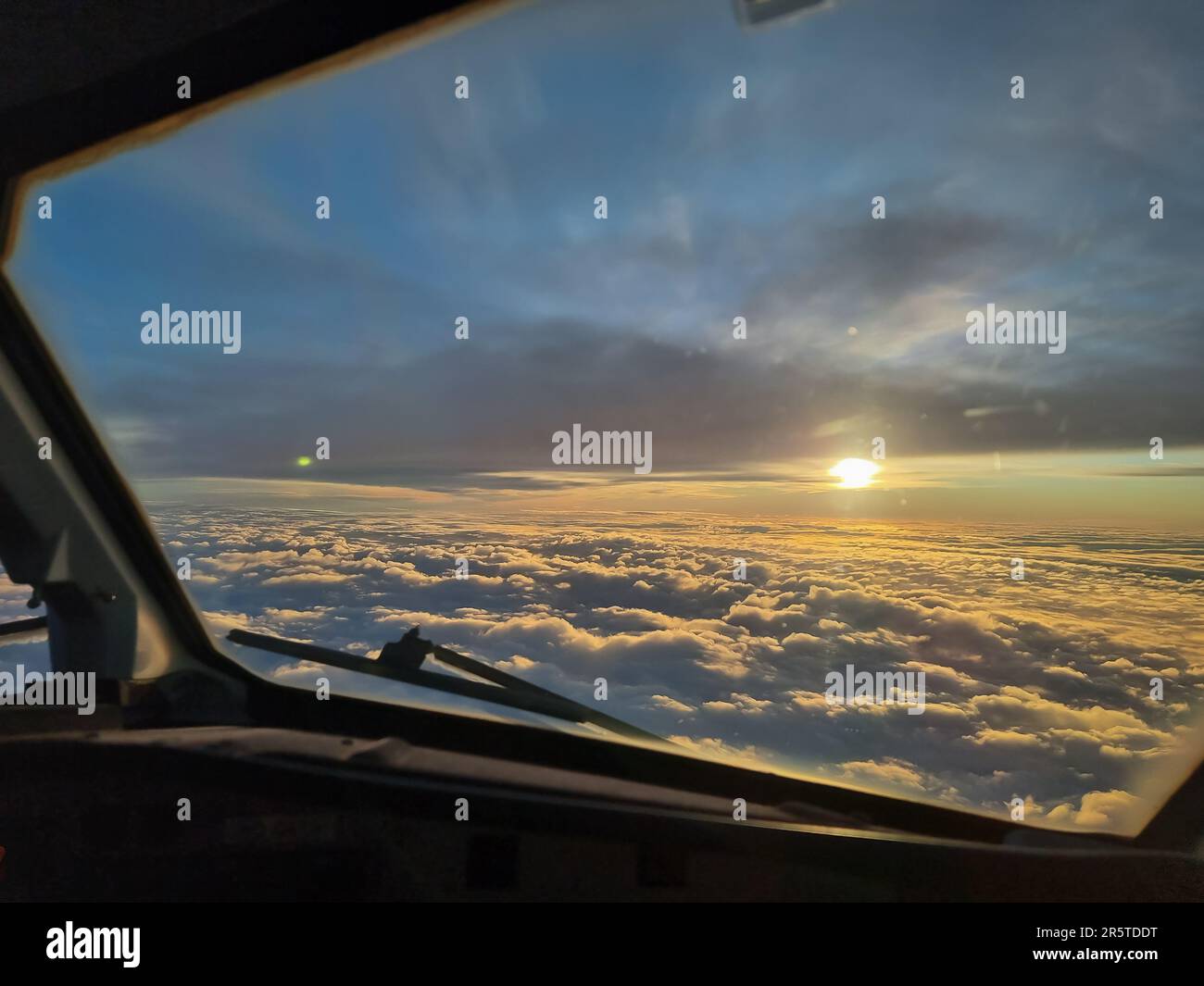 Aerial view of a sunrise, illuminating the clouds from the perspective of an airplane cockpit ...